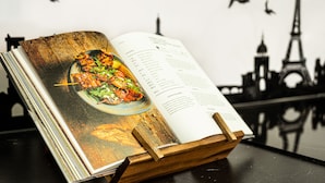 Um livro aberto com uma paisagem urbana ao fundo, possivelmente um menu ou guia, apoiado em uma superfície refletora.