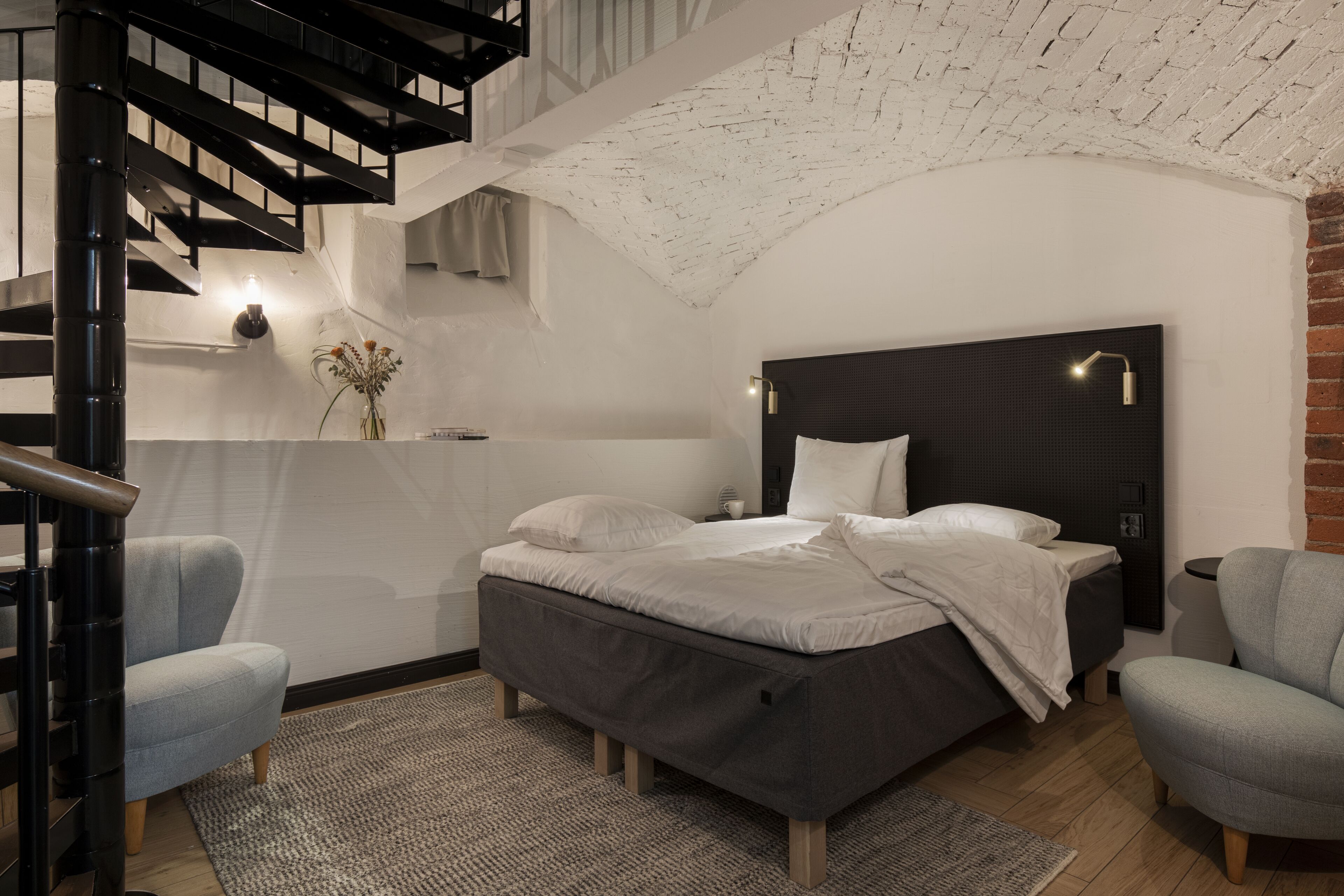 Quarto moderno com uma cama grande, cabeceira preta, escada e parede de tijolos.
