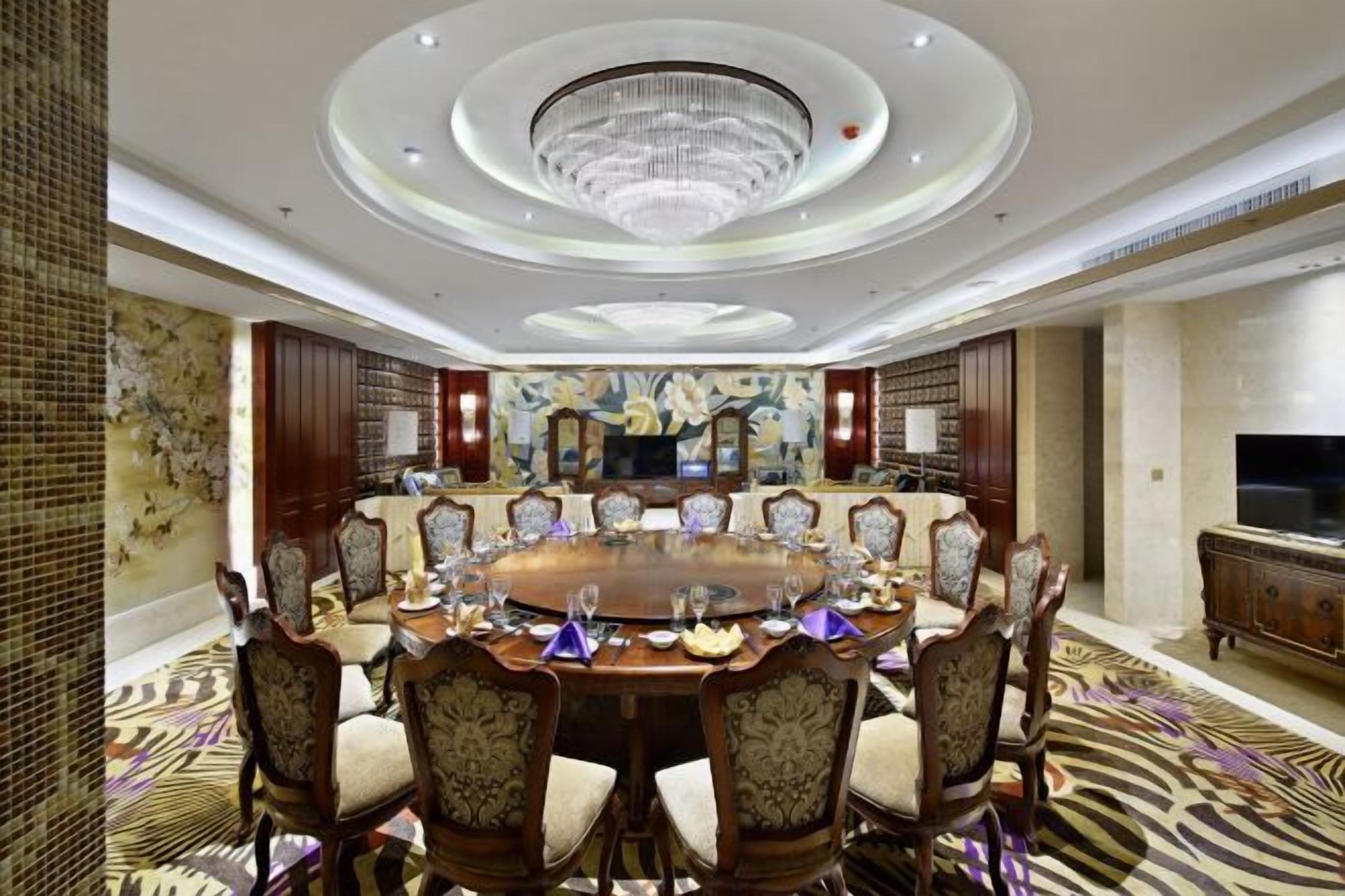 Uma sala de conferências com uma mesa redonda, cadeiras, um candelabro e uma televisão.