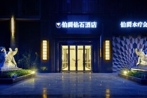 Entrada de hotel com piso refletivo, duas estátuas iluminadas e um grande design de parede em formato de leque.