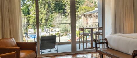 Quarto de hotel com uma grande porta de correr de vidro que dá para área externa com piscina e cadeiras.