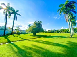 Um campo de golfe bem cuidado, com caminhos definidos, palmeiras e um edifício ao fundo.