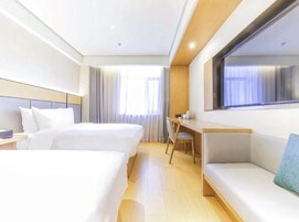 Quarto de hotel com duas camas, uma escrivaninha, uma cadeira e um sofá.