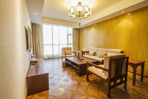 Quarto de hotel com piso de madeira, um sofá, uma mesa de centro, uma televisão e uma escrivaninha.