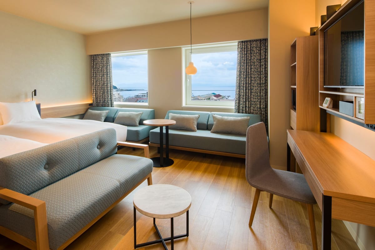 Quarto de hotel com uma cama, dois sofás, uma mesinha e uma televisão.