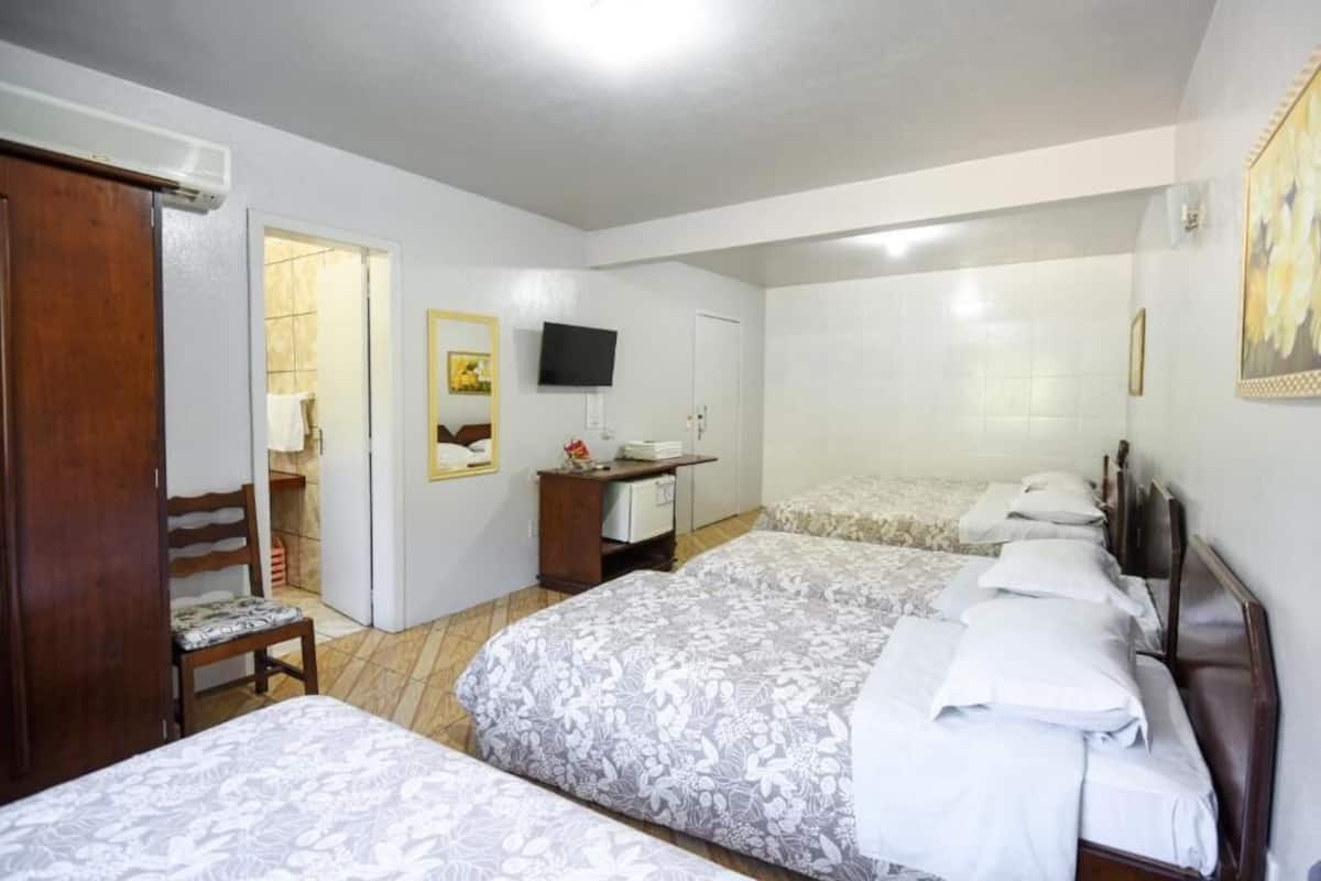 Quarto de hotel com duas camas, uma escrivaninha, uma cadeira, uma TV e uma porta para um banheiro.