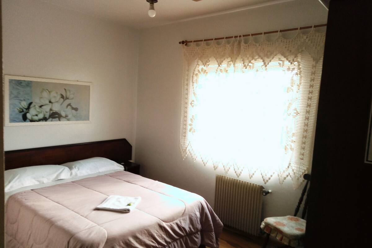 Quarto com cama, uma cadeira, radiador e ventoinha no teto.