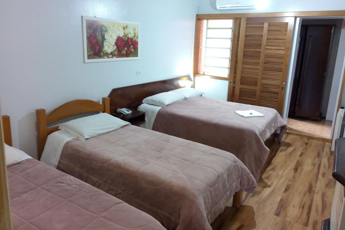 Quarto de hotel com duas camas, cabeceira de madeira, mesa de cabeceira com telefone, pintura na parede e janela com vista.