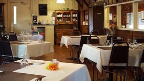 Restaurante com várias mesas preparadas para refeições, vigas de madeira no teto e um quadro de menu na parede.