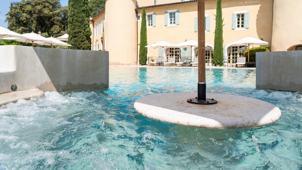 Uma banheira de hidromassagem cercada por uma piscina, com um edifício ao fundo.