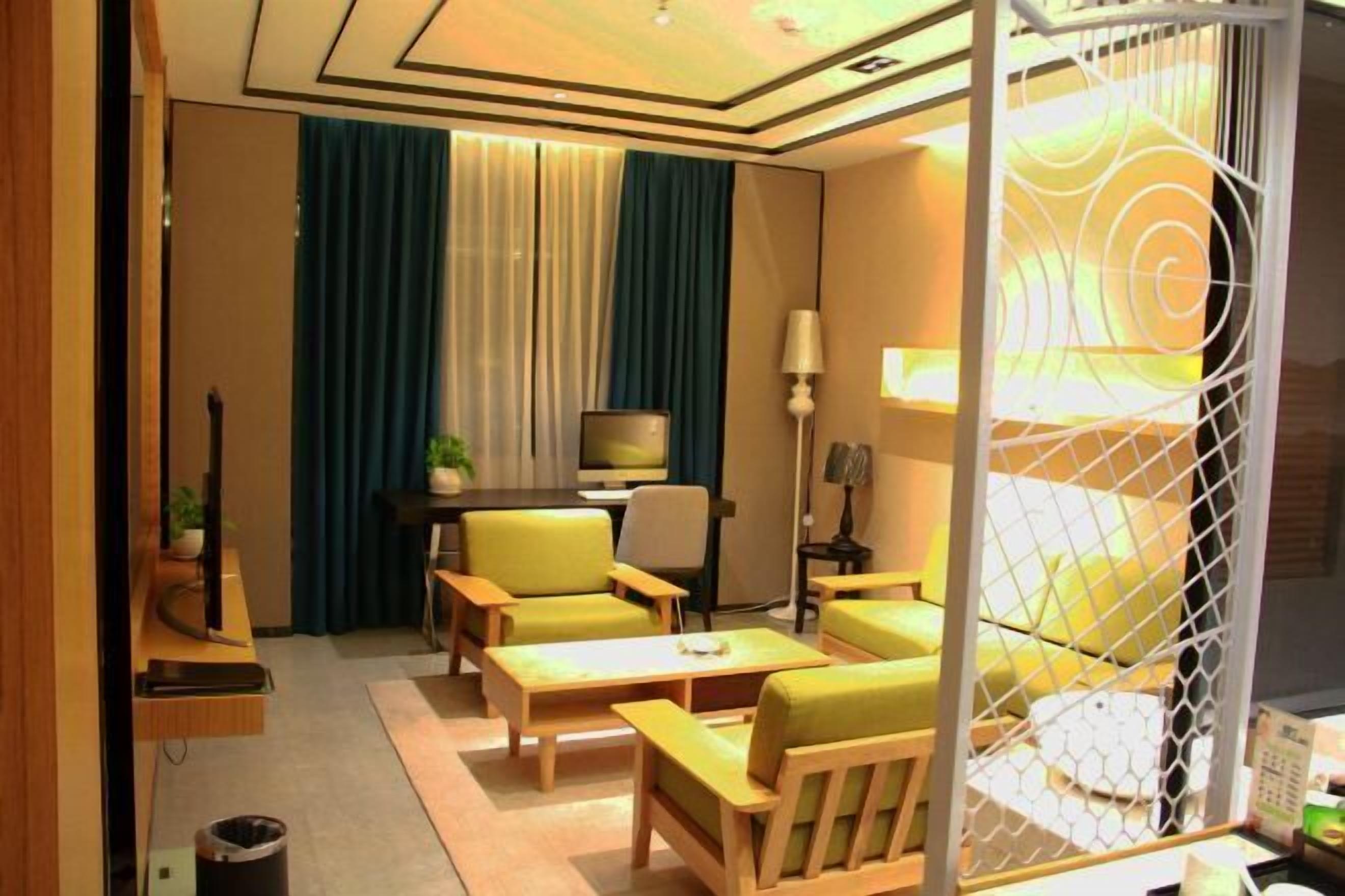 Quarto de hotel com escrivaninha, televisão, cama com cabeceira branca e área de estar com cadeiras e mesa.