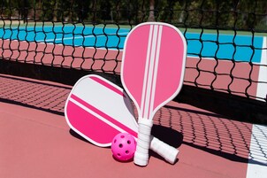 Uma quadra de tênis com rede, duas raquetes e uma bola.
