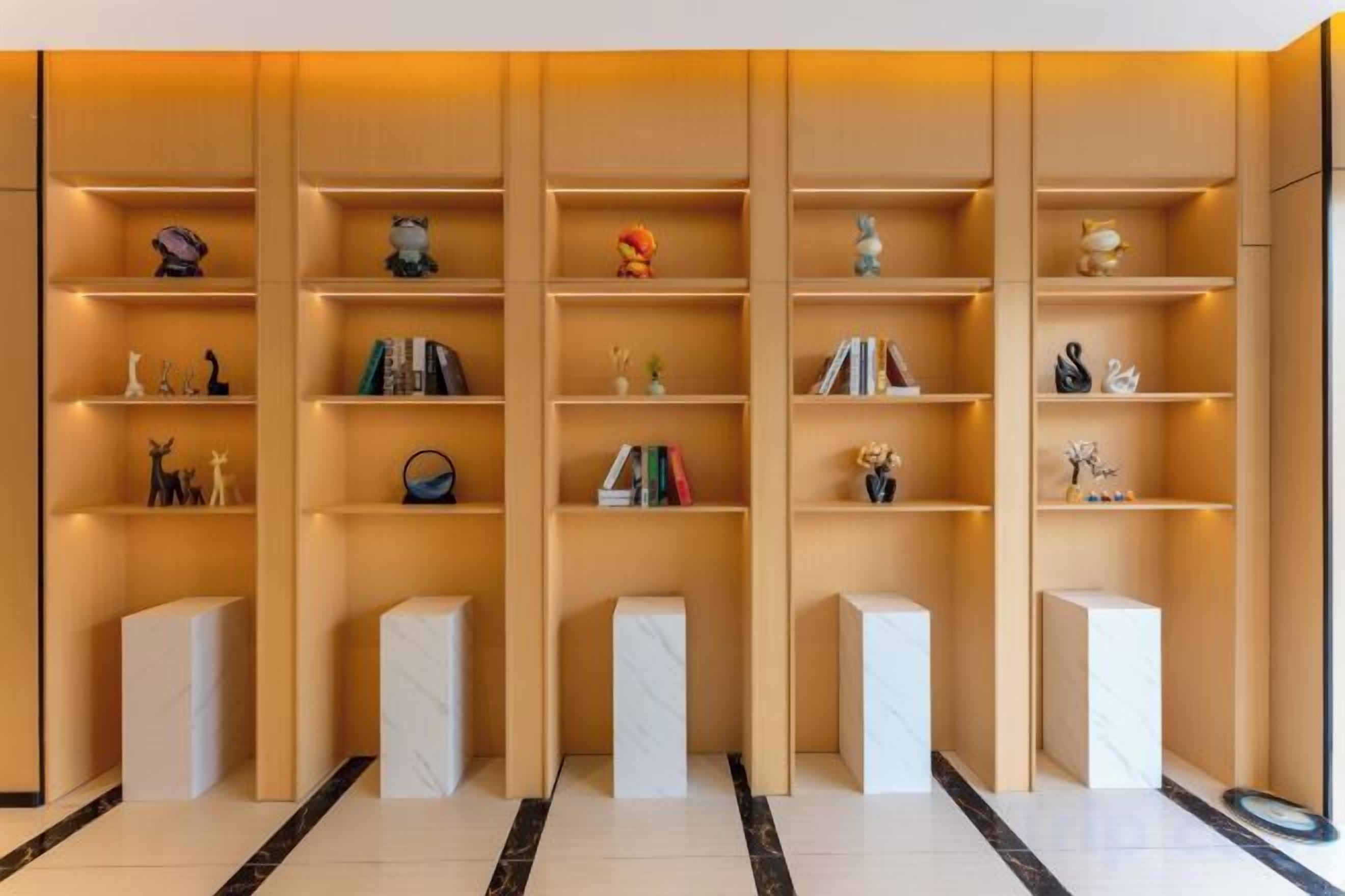 Um hall de hotel com design moderno, destacando um pilar central, diversas prateleiras com objetos decorativos e piso de mármore.