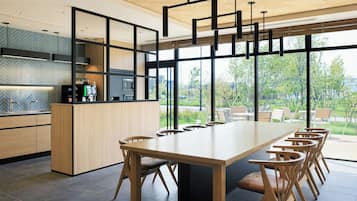 Cozinha moderna com uma grande mesa de jantar e cadeiras, janelas amplas com vista para o verde, e teto de madeira.