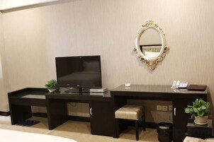 Quarto de hotel com televisão, escrivaninha, cadeira e espelho na parede.