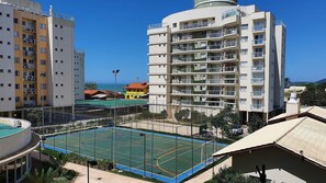 Um edifício residencial com vários andares, varandas, quadra de tênis e vista ampla para o mar.
