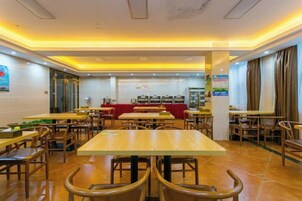 Restaurante com várias mesas e cadeiras, um balcão com alimentos e toalha de mesa vermelha.