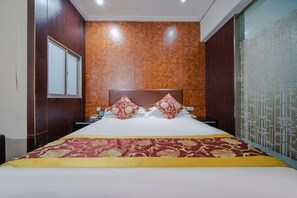 Quarto de hotel com uma cama grande, cabeceira de madeira, janela e um painel decorativo na parede.