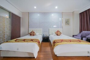 Quarto de hotel com duas camas, uma mesinha de cabeceira, uma cadeira e um espelho grande.