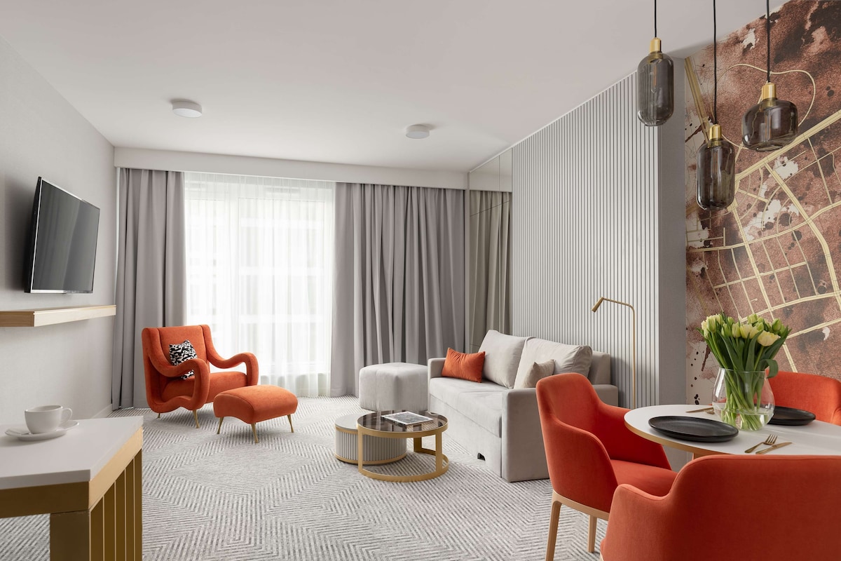 Uma sala de estar moderna com sofá, poltronas, mesa de centro e área de jantar com mesa posta para dois.