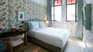 Quarto com cama, escrivaninha com cadeira, quadro emoldurado e janela com cortinas.