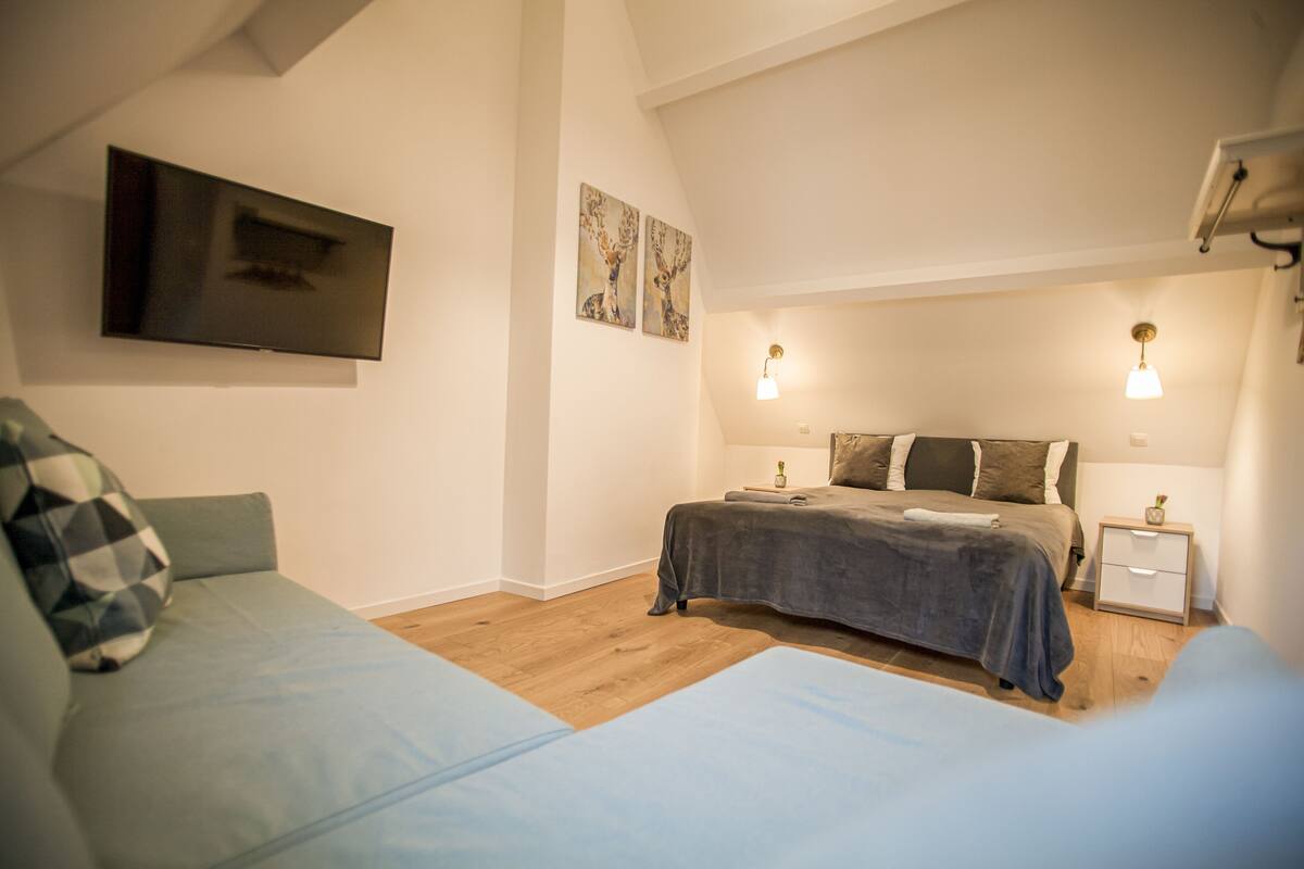 Um quarto com cama, mesa de cabeceira, televisão montada na parede e duas luminárias de parede.