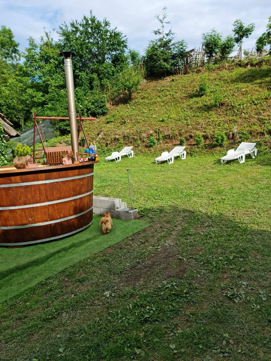 Uma grande estrutura de barco de madeira com chaminé, rodeada por uma área gramada com espreguiçadeiras brancas.