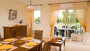 Uma área de refeições com uma mesa posta para quatro pessoas, um sofá e uma janela com cortinas.