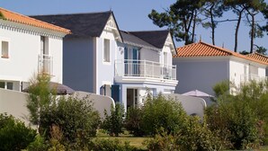 Um edifício residencial de dois andares com varanda, rodeado por vegetação e árvores.
