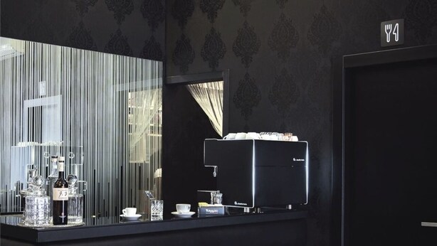 Uma área de recepção de hotel moderna com balcão preto, uma máquina de café e um espelho.