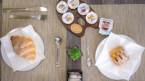 Disposição para o café da manhã com croissants, uma tábua de frutas e diversos acompanhamentos.