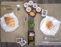 Disposição para o café da manhã com croissants, uma tábua de frutas e diversos acompanhamentos.