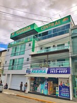 Um edifício com uma placa verde que diz "POUSADA CENTRAL" e uma farmácia chamada "FARMA" com uma placa azul.
