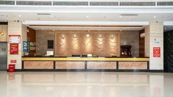 Recepção de hotel com balcão de mármore, painel informativo fixado na parede e sinal de segurança contra incêndio.