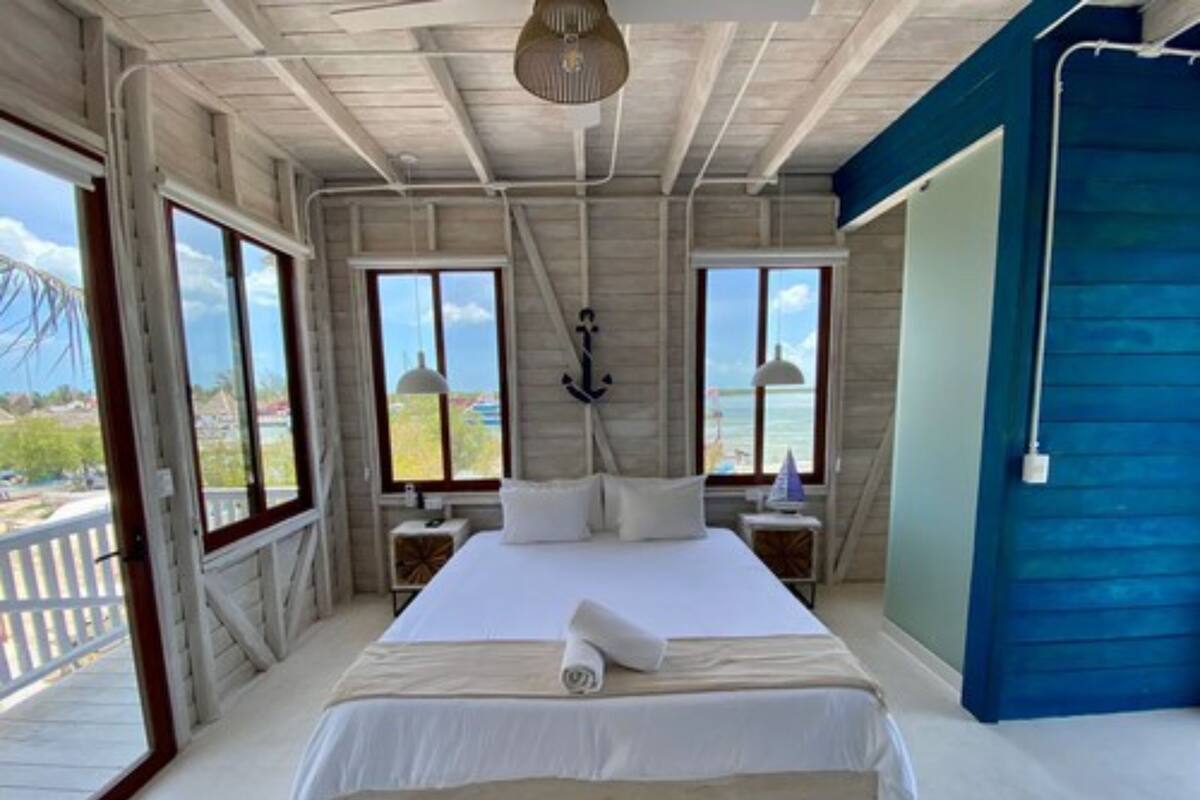 Quarto com uma cama grande, duas mesas de cabeceira, vista para a praia e uma porta azul.