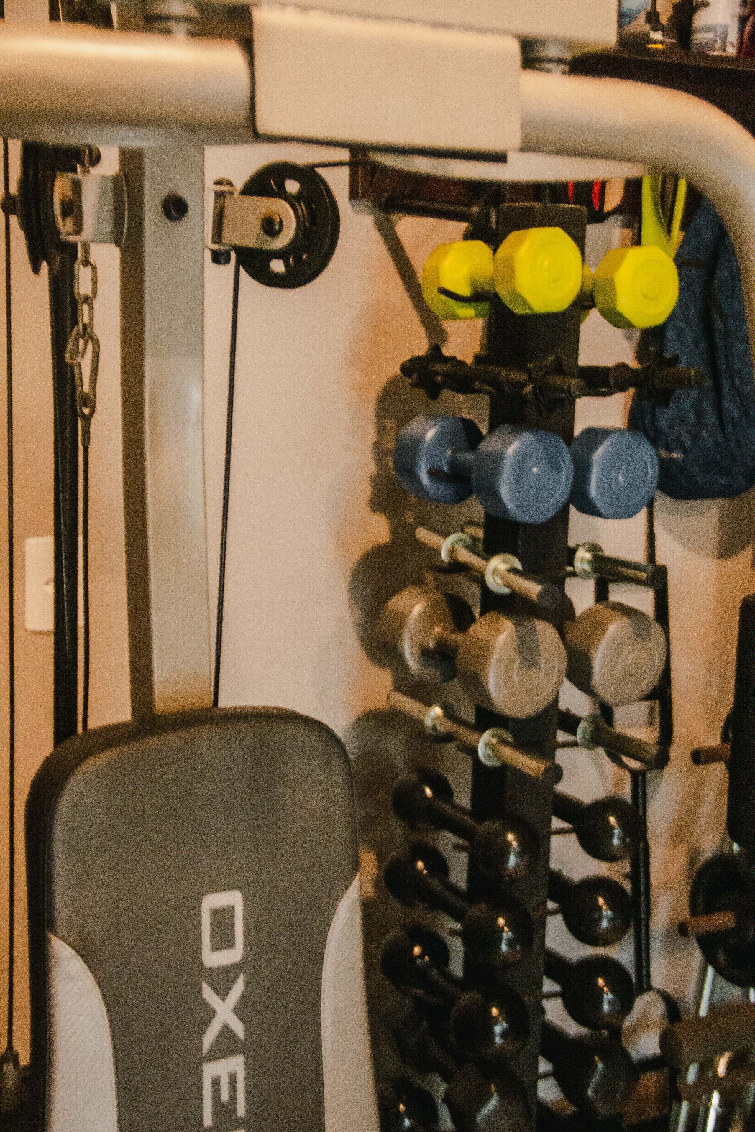 Uma academia com um suporte de halteres fixado na parede, um banco de musculação e uma toalha pendurada em um porta-toalhas.