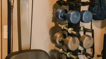 Uma academia com um suporte de halteres fixado na parede, um banco de musculação e uma toalha pendurada em um porta-toalhas.