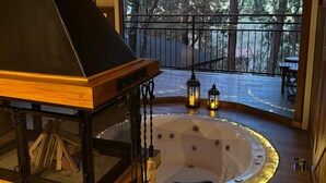 Um espaço interior acolhedor com lareira a lenha, hidromassagem e um deck com área de estar ao ar livre.