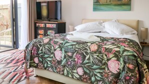 Quarto de hotel com cama, televisão, quadro na parede e vista para o exterior.