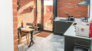 Uma cozinha compacta com parede de tijolos, uma área de refeições com mesa e cadeiras, e uma janela pequena.
