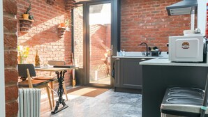 Uma cozinha compacta com parede de tijolos, área de refeições com uma cadeira e mesa, e um forno a pizza.
