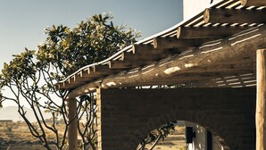 Uma estrutura de pérgola de madeira com um muro de tijolos e uma porta em arco.