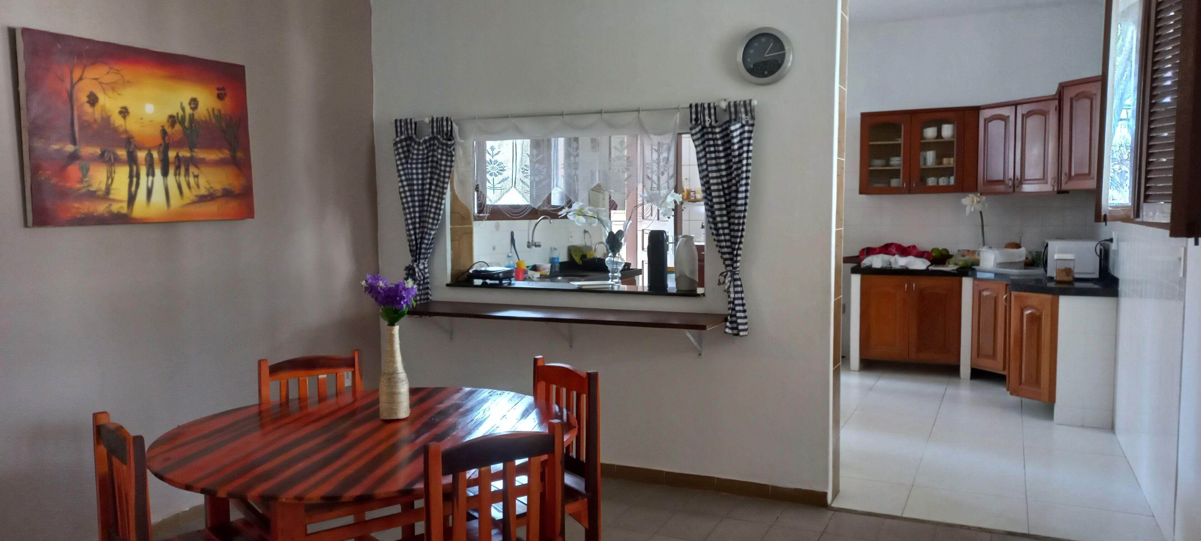 Uma sala de jantar com uma mesa e cadeiras de madeira, um vaso com flores e uma janela com cortinas.