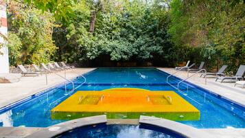 Piscina com plataforma flutuante, rodeada por árvores e espreguiçadeiras.