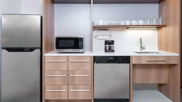 Uma cozinha compacta com geladeira de aço inoxidável, micro-ondas, cafeteira e lava-louças.
