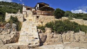 Uma escadaria de pedra leva a um edifício com telhado de colmo, cercado por terreno rochoso e vegetação.
