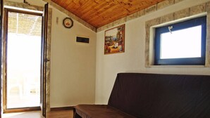 Quarto com teto de madeira, sofá marrom, janela com moldura azul e um quadro na parede.