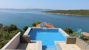 Piscina com vista para o mar e colinas.