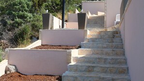 Uma escadaria de pedra serpenteia subindo uma colina, com paredes brancas e um jardim na base.