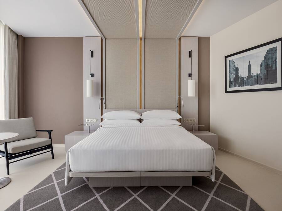 Quarto de hotel moderno com uma cama grande, uma escrivaninha, uma cadeira e uma pintura da paisagem urbana na parede.
